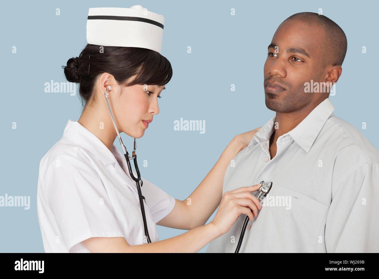 Female doctor listening the heartbeat of male patient over light blue ...