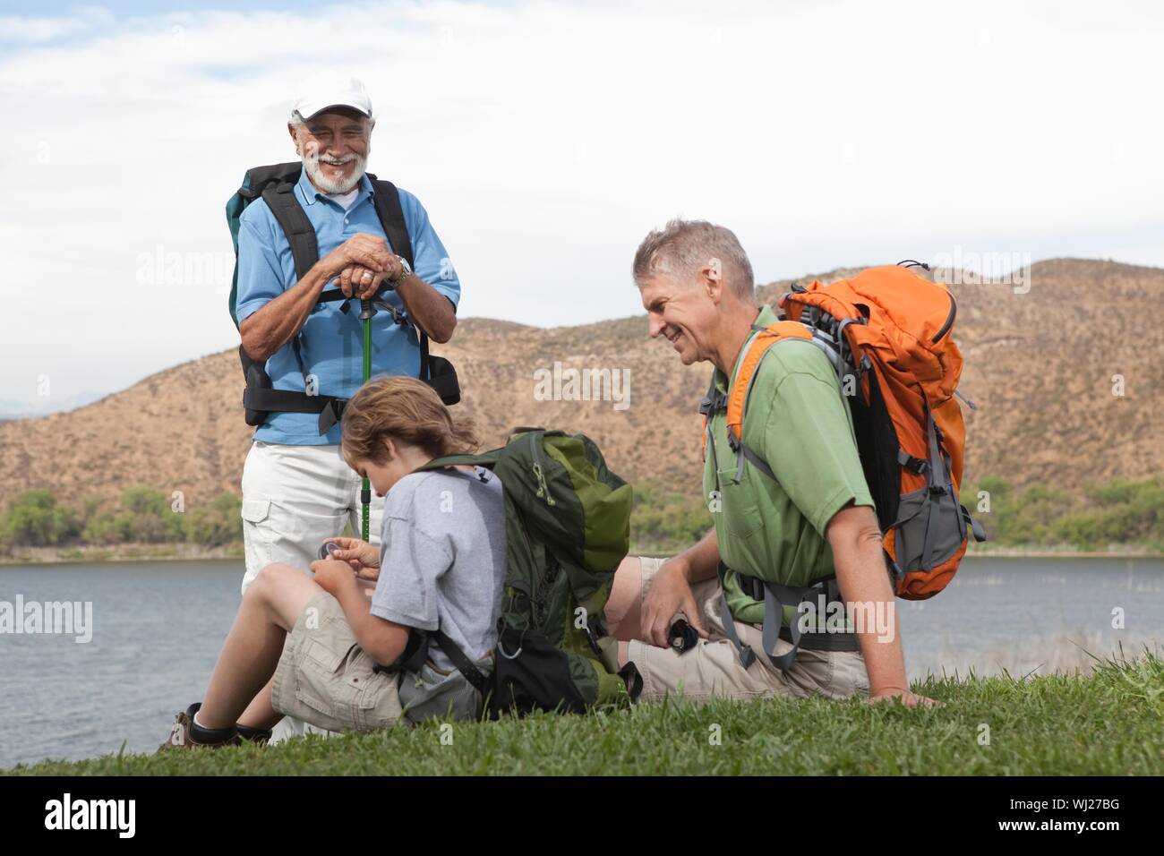 Father, son and grandson with backpacks sitting by the lake Stock Photo ...