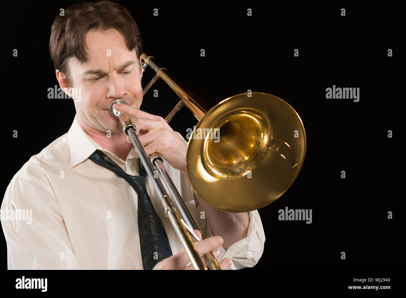 Caucasian man playing music using trombone isolated over black ...