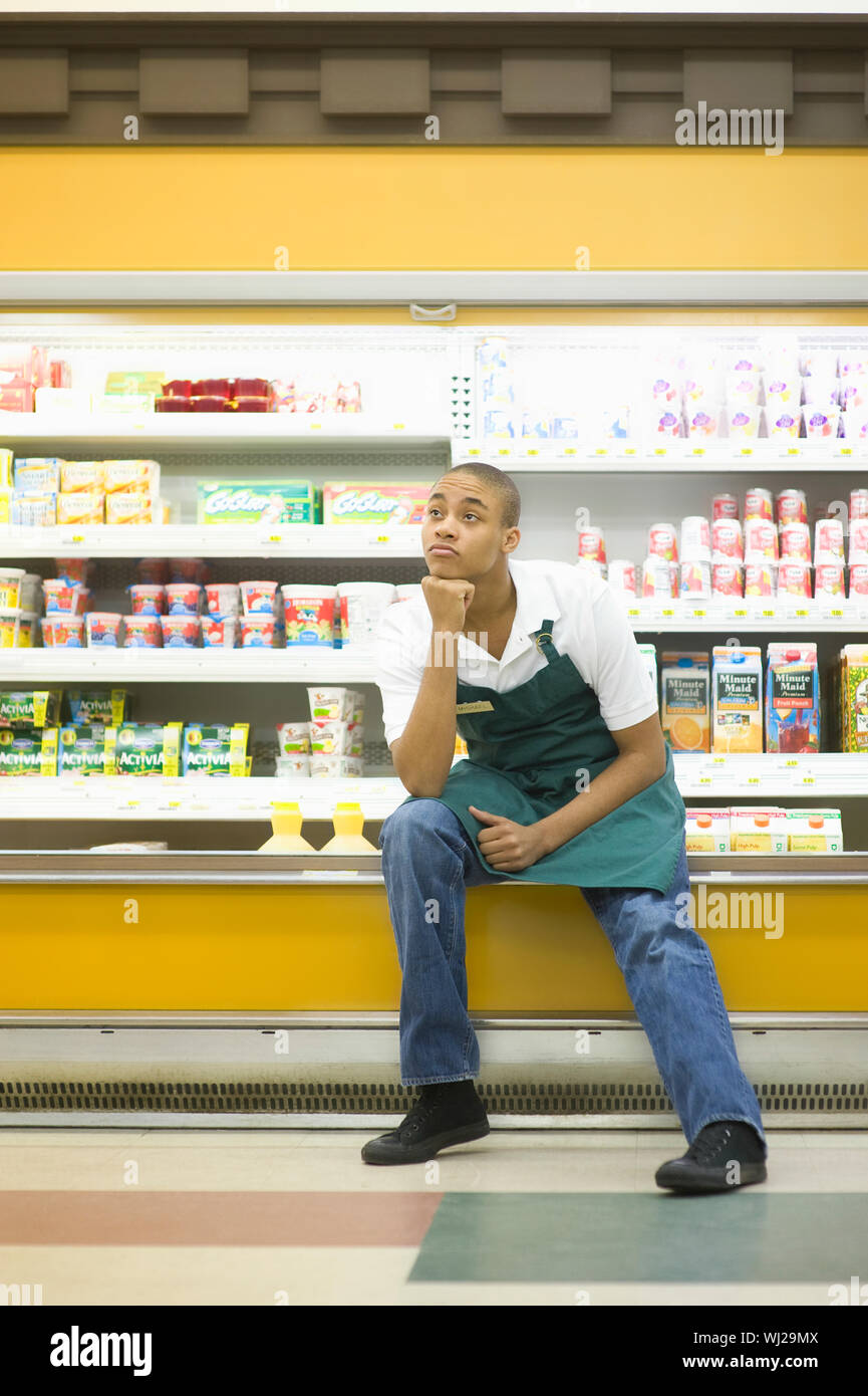 Bored male teenage employee sitting at supermarket fridge Stock Photo ...