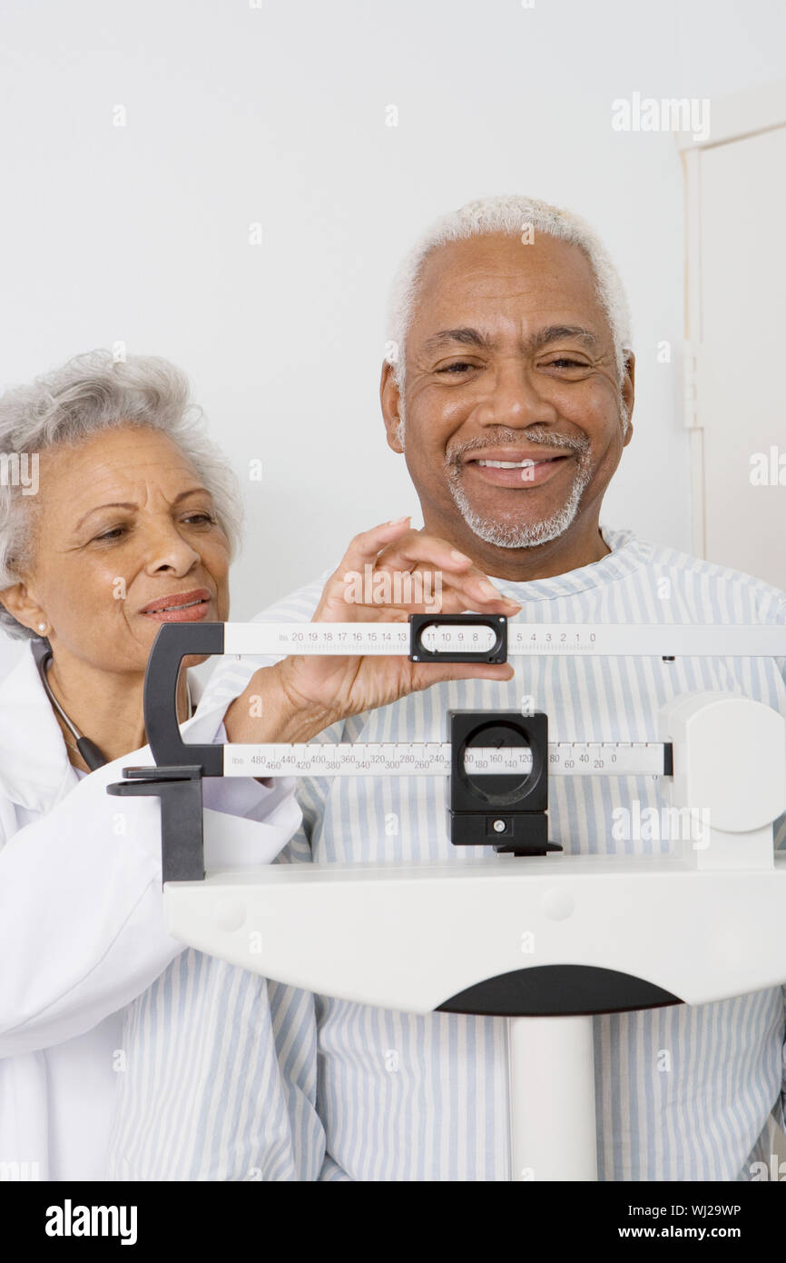 Portrait of a happy senior male patient standing on weight scale with ...
