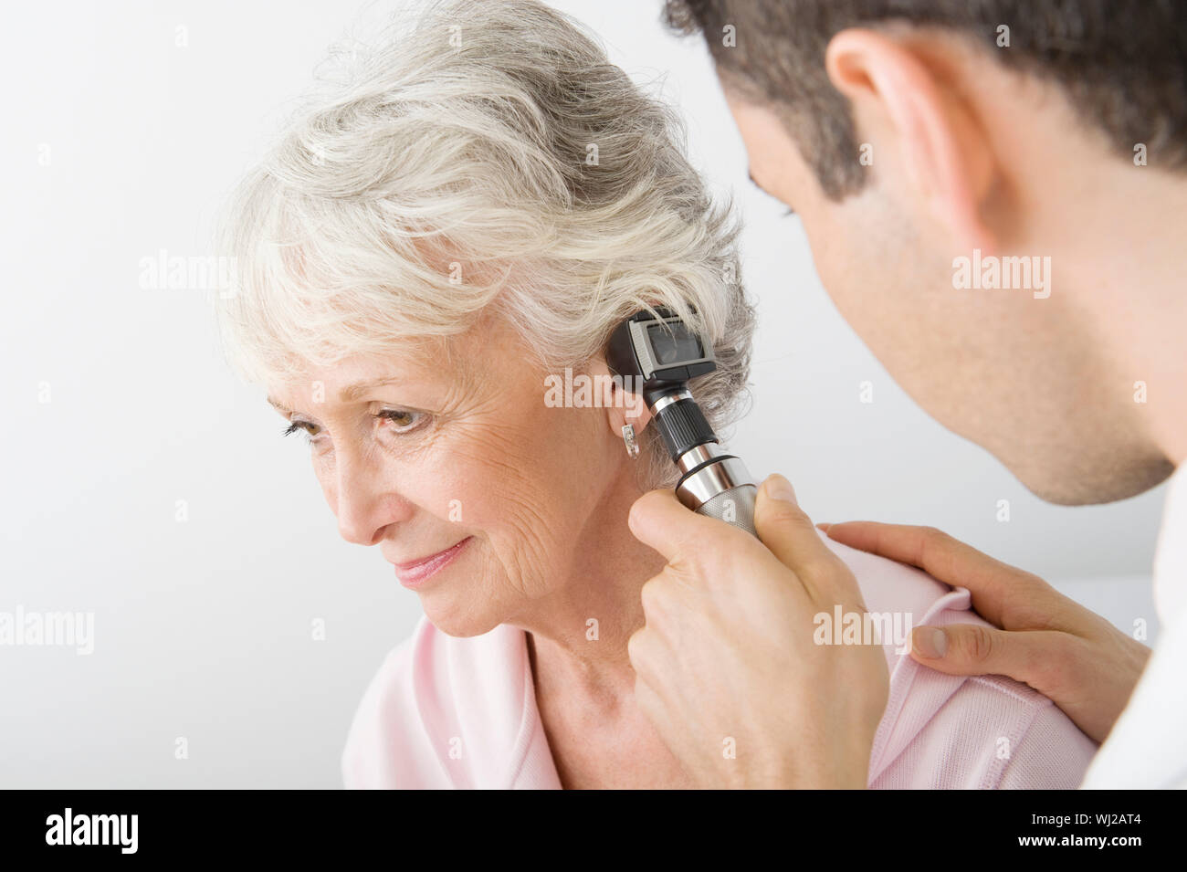 Mature male doctor examining patient's ear using otoscope in clinic ...