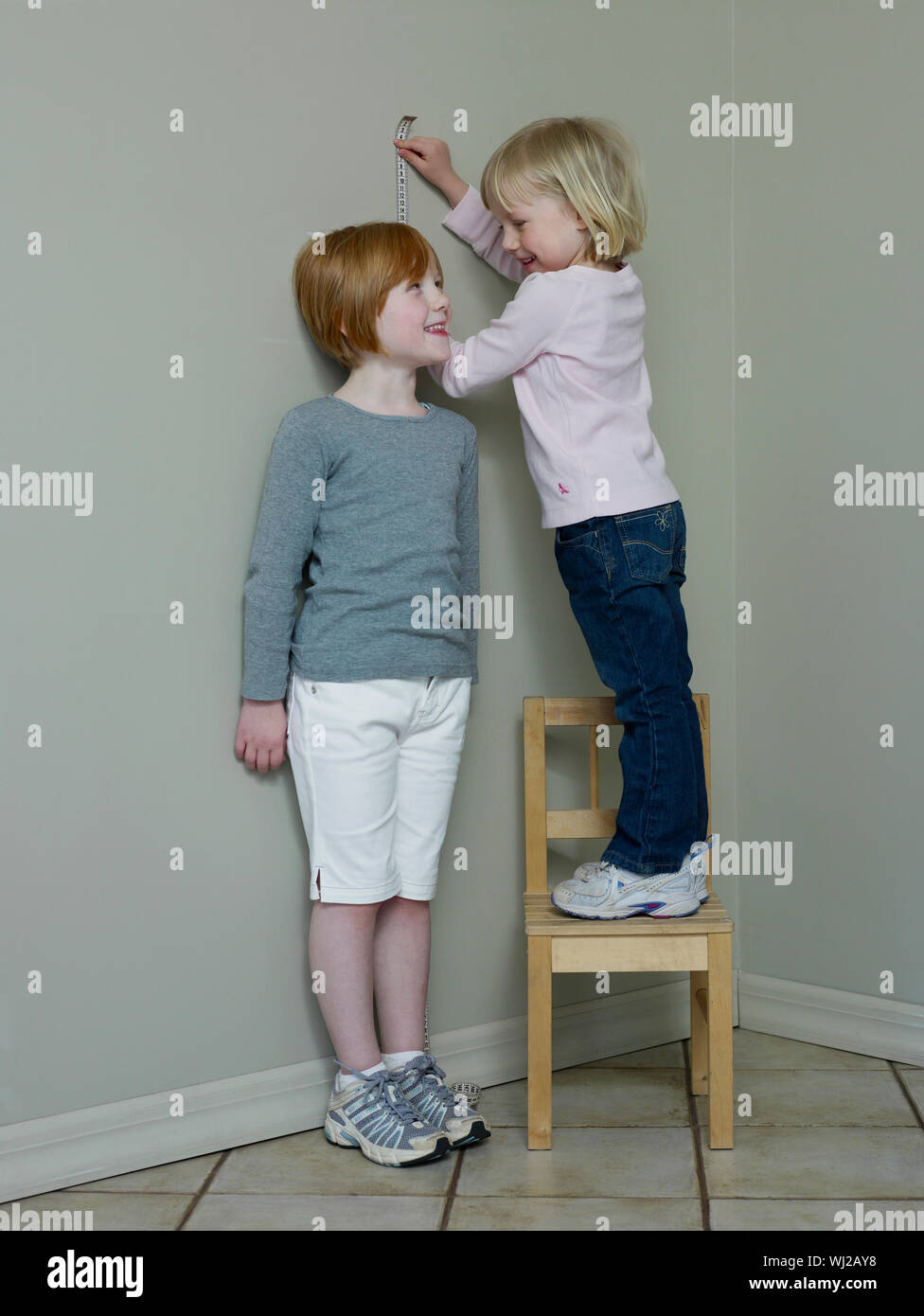 Full length of two girls measuring height against wall Stock Photo - Alamy