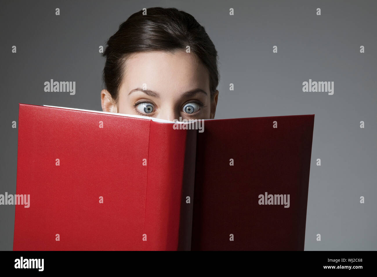 An astonished young female reading book with eyes wide open isolated ...