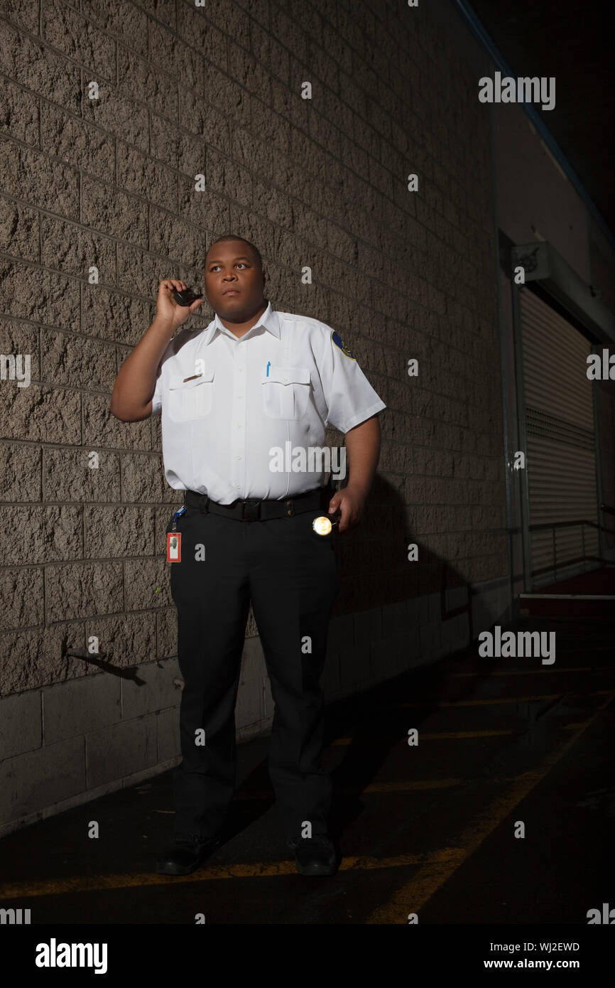 Young mixed race security guard communicating on walkie talkie while ...