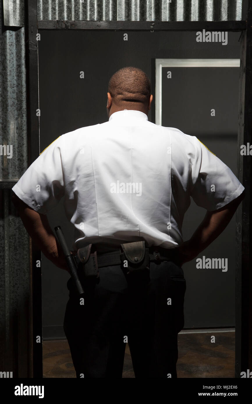 Rear view of a young security guard standing in front of the corrugated ...