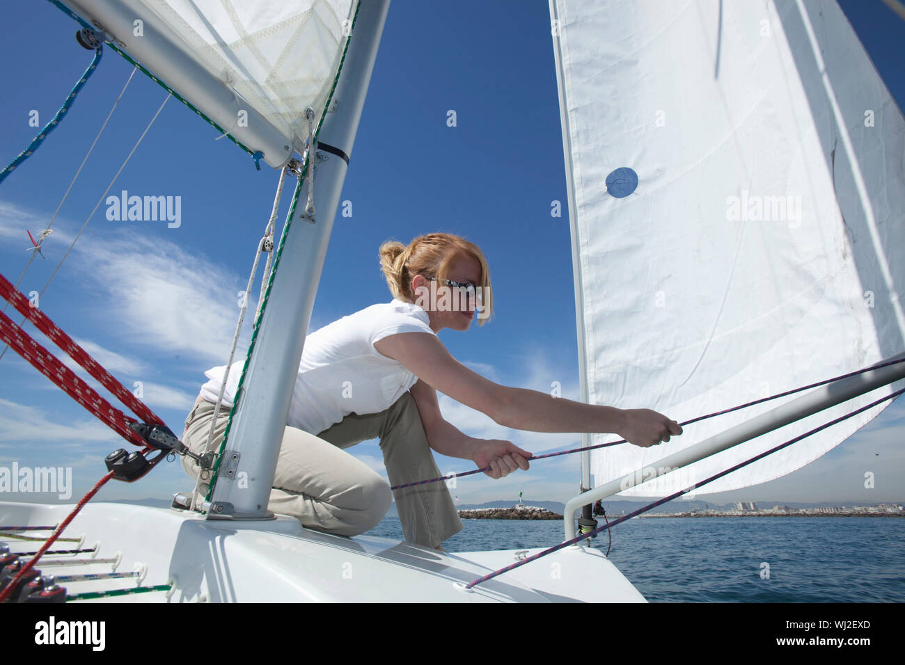 Side view of a young female pulling rope while sailing on sailboat ...