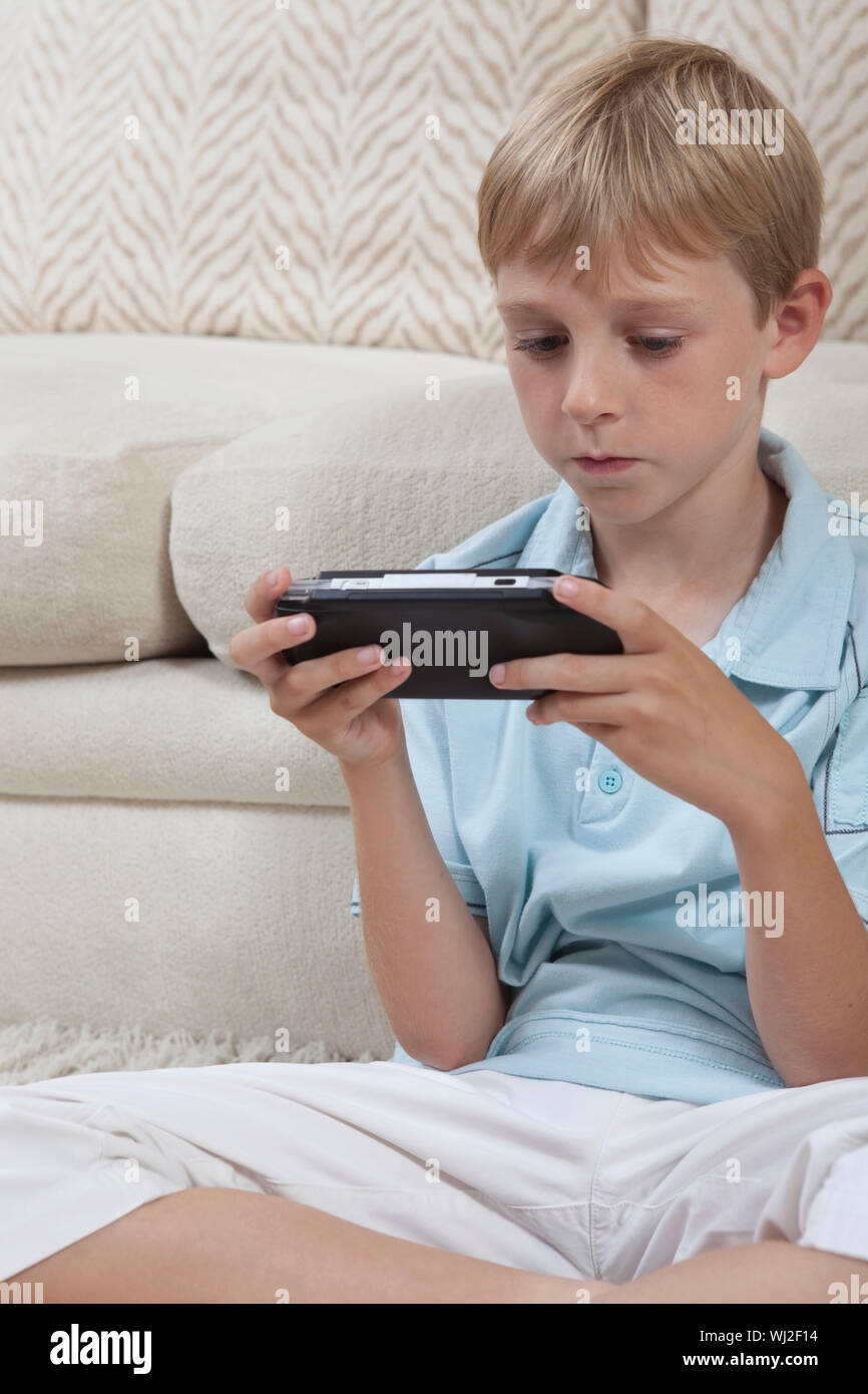 Little boy playing games on PSP while sitting on floor at home Stock ...