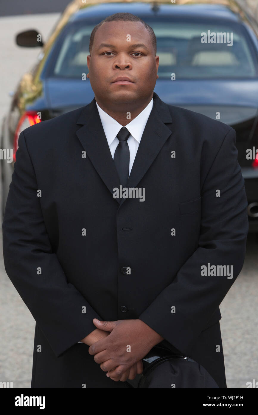 Portrait of mixed race serious male chauffeur with car in background ...
