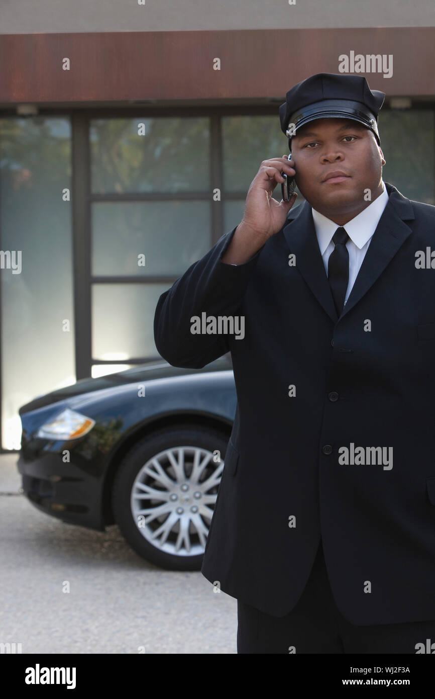 Portrait of a serious male chauffeur on a call with car in background ...