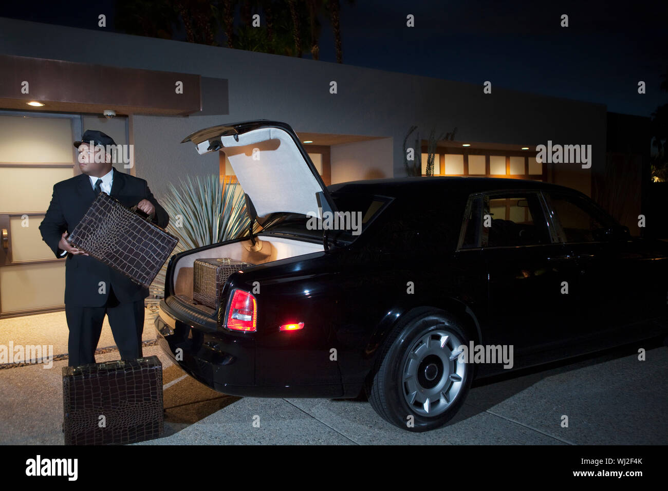 Chauffeur loading luggage in car while standing at driveway Stock Photo ...