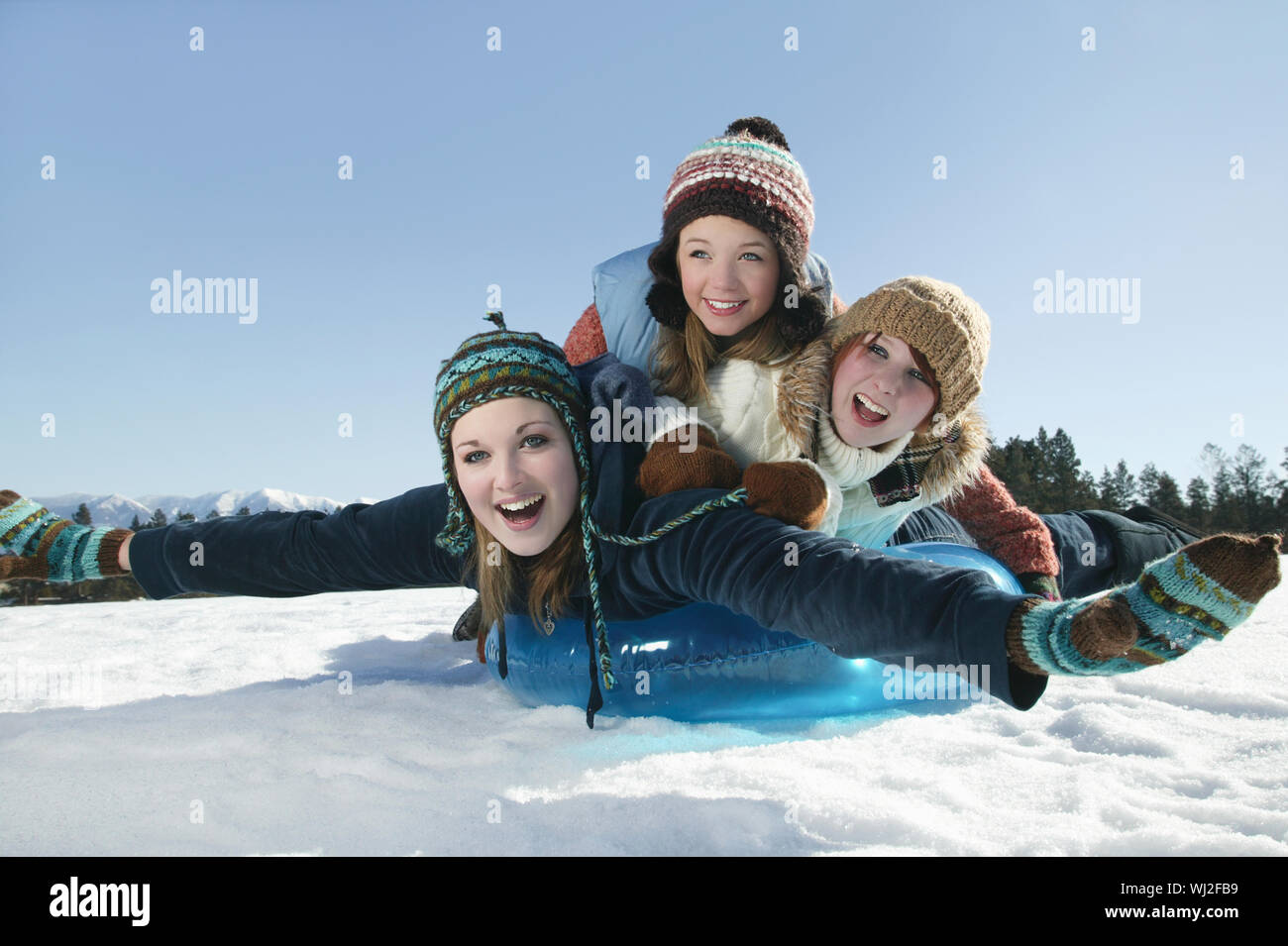 Three female friends sledding at winter time Stock Photo - Alamy