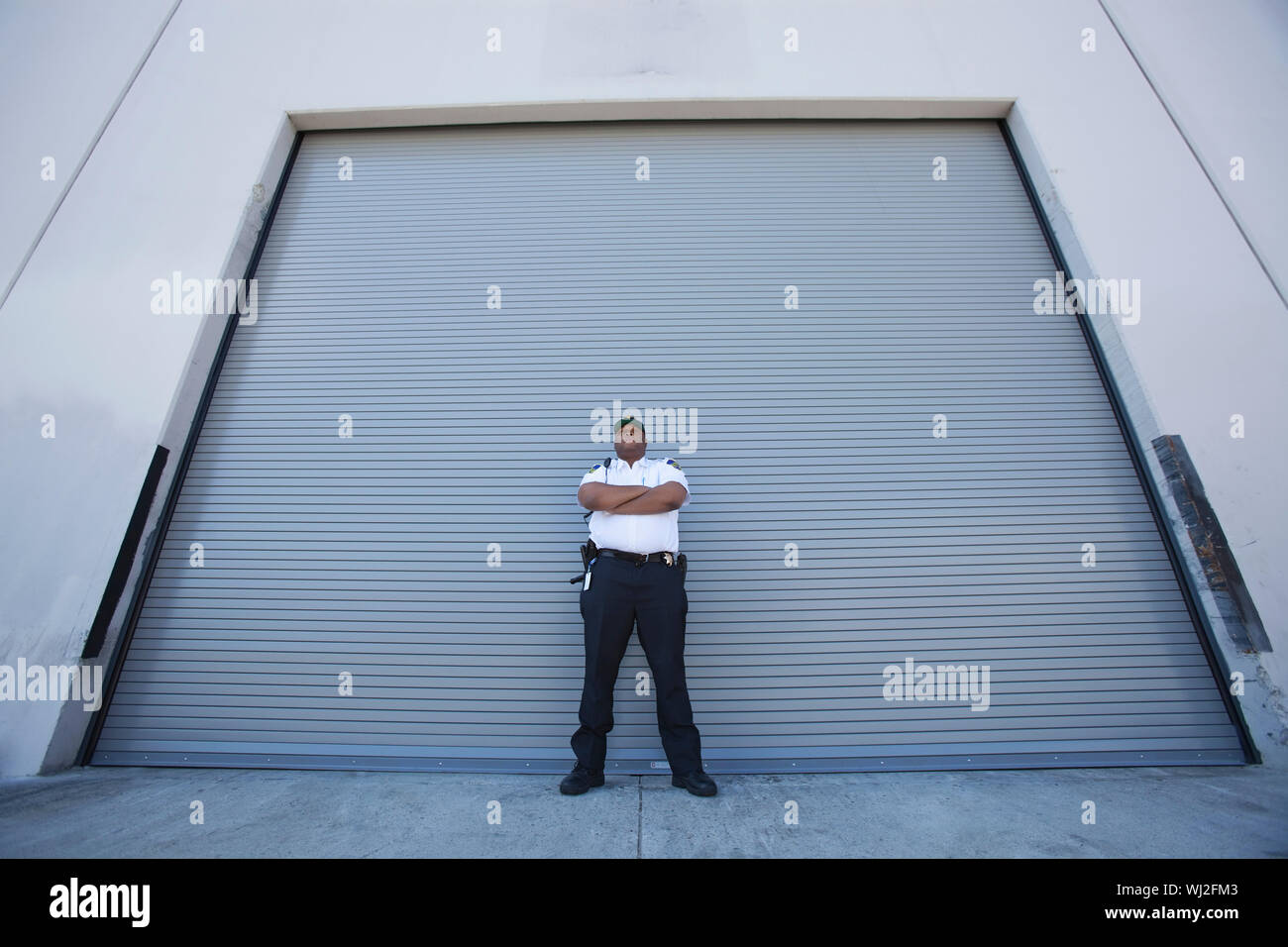 Low angle view of a young security guard standing with arms crossed in ...
