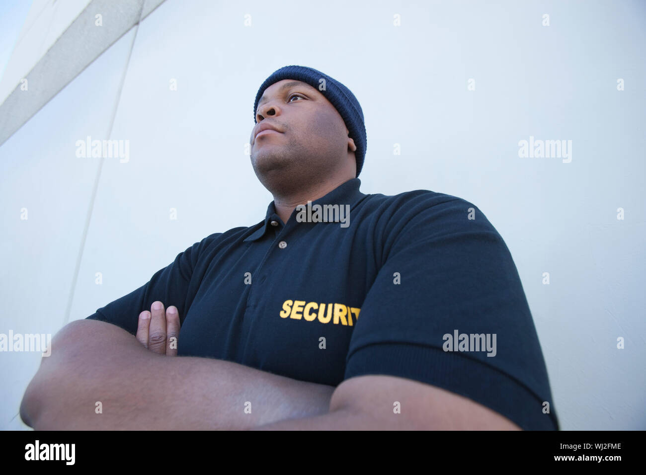 Low angle view of a young security guard standing with arms crossed by ...