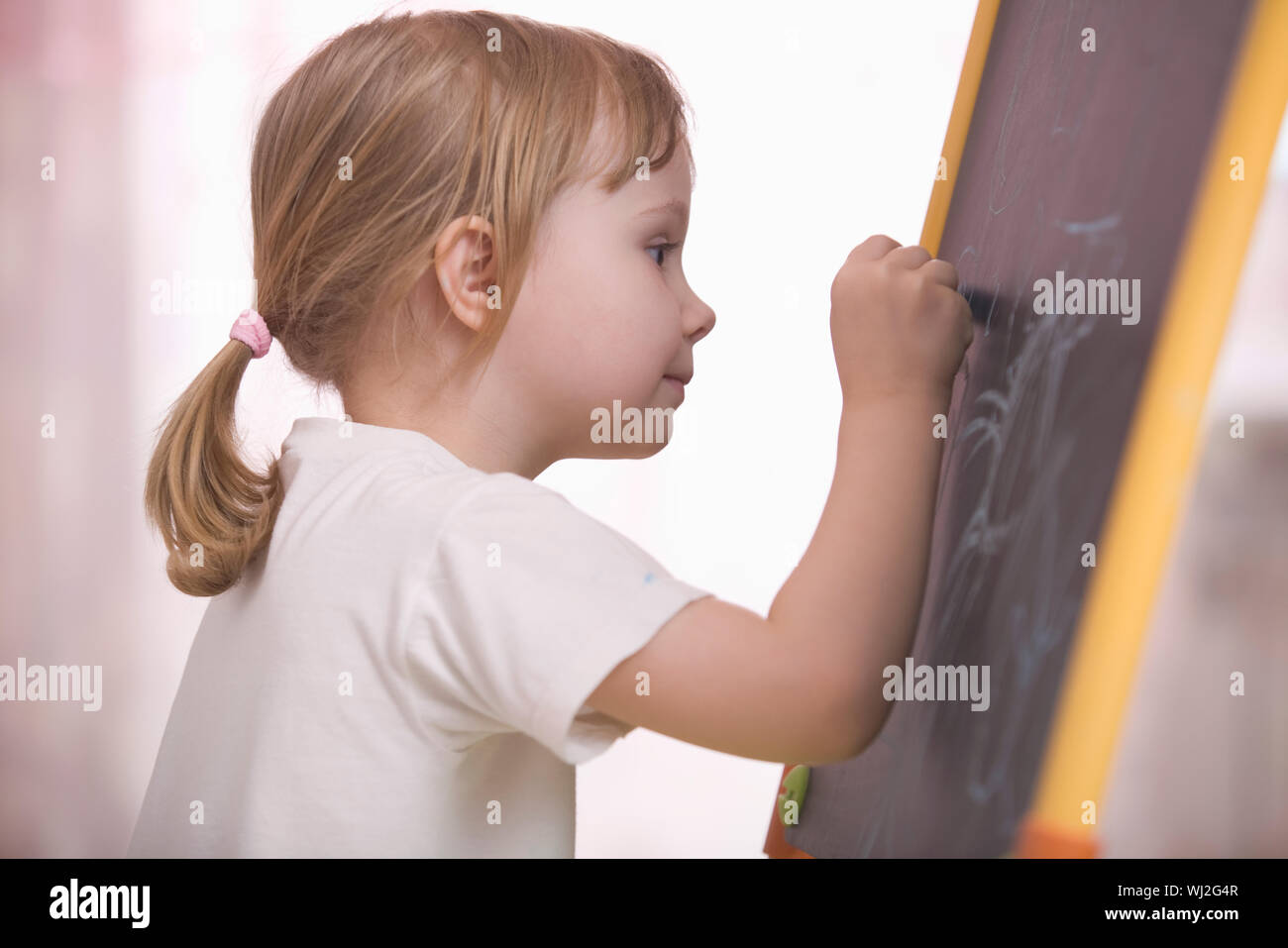 Side view of cute little girl drawing on chalkboard at home Stock Photo ...