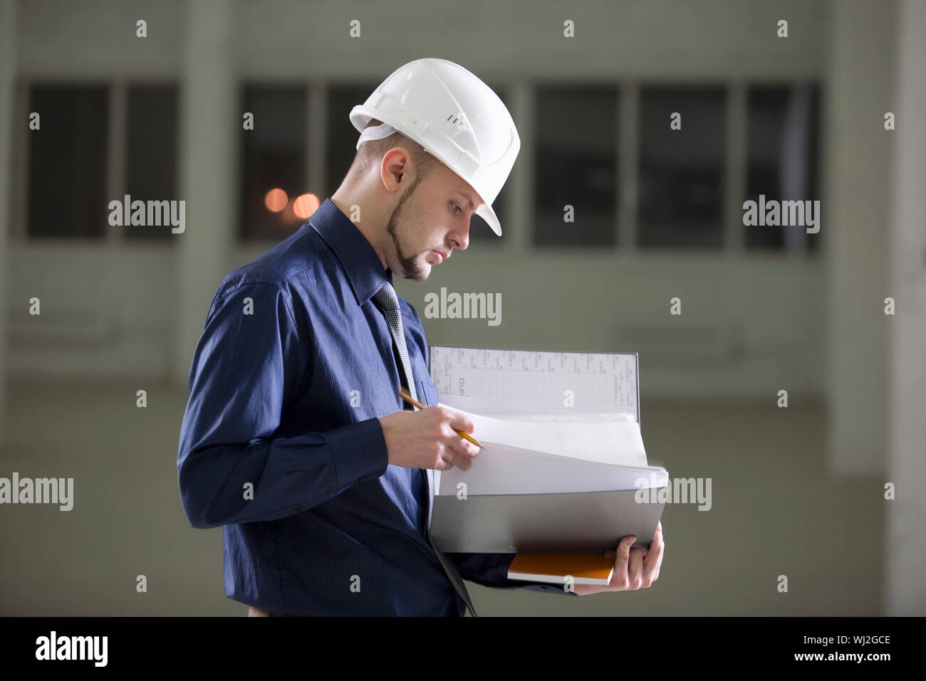 Side view of young male architect going through file folder in ...