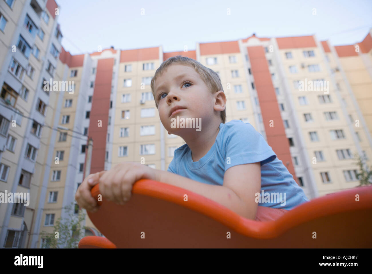 Low angle view of cute little boy in playground with residential ...