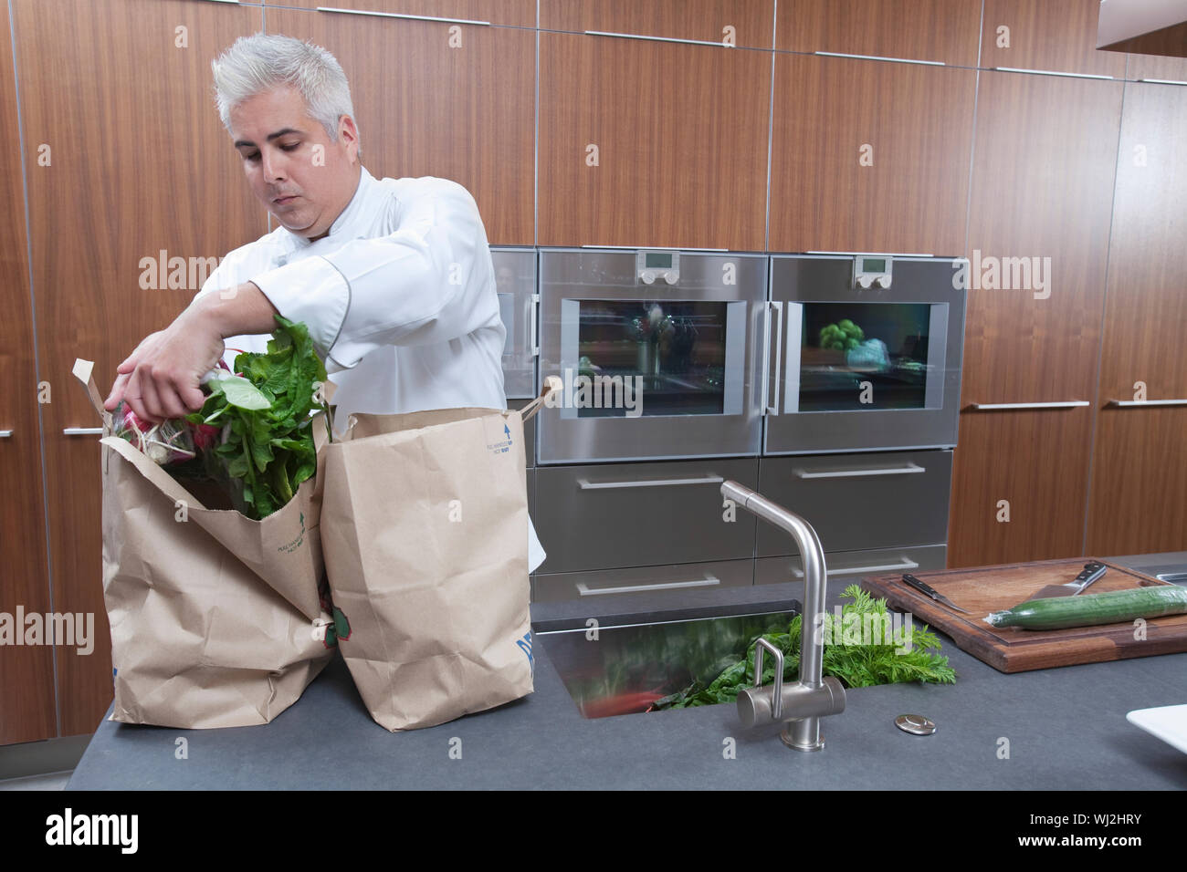 Male chef unpacking groceries from paper bags in commercial kitchen ...
