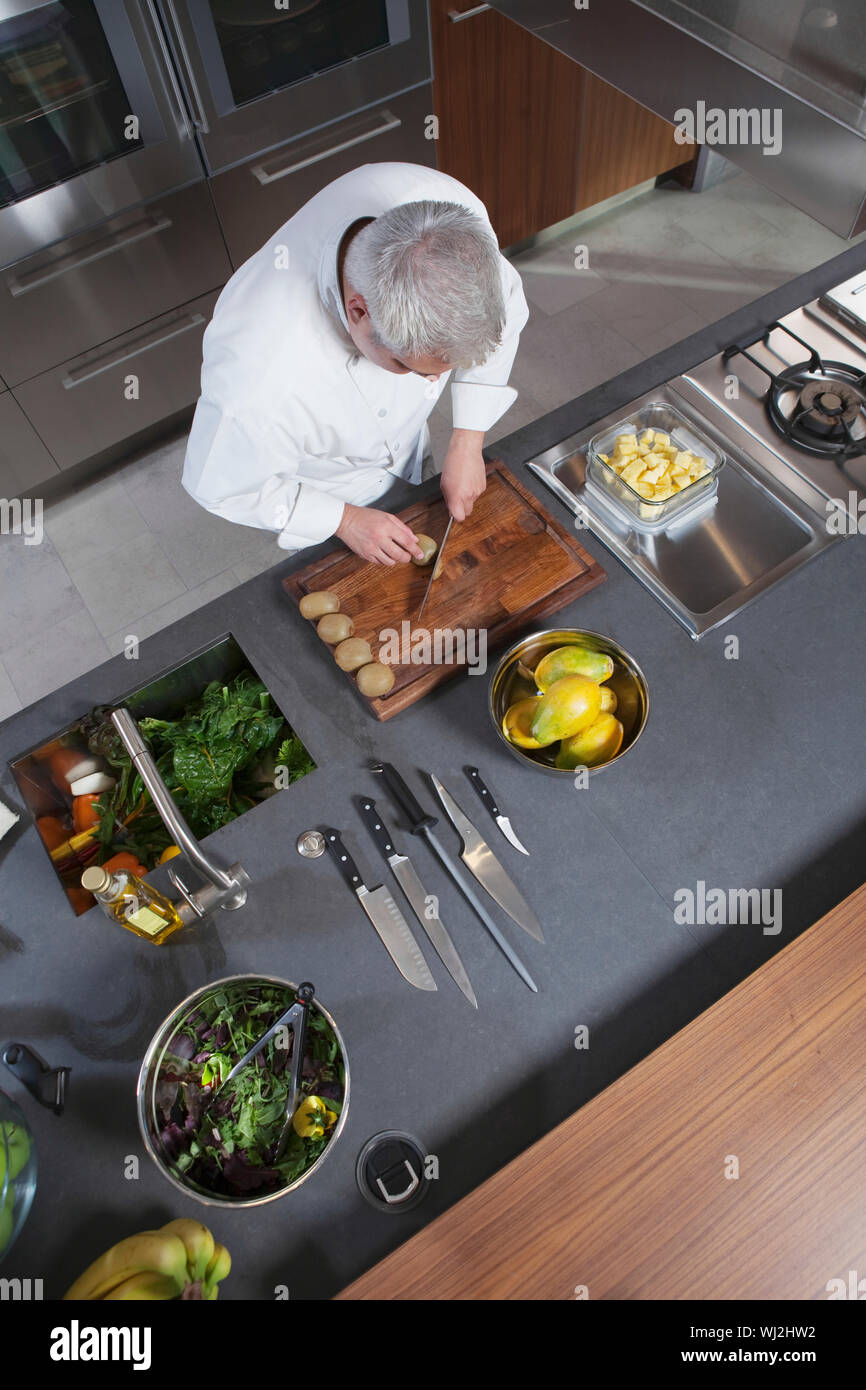 High angle view of male chef chopping kiwi on board at commercial ...