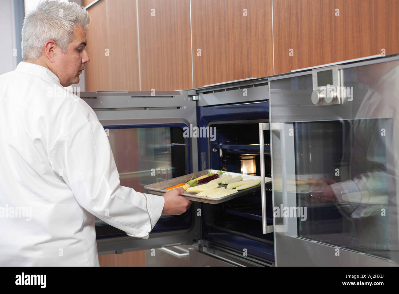 Side view of male chef placing baking tray in oven Stock Photo - Alamy