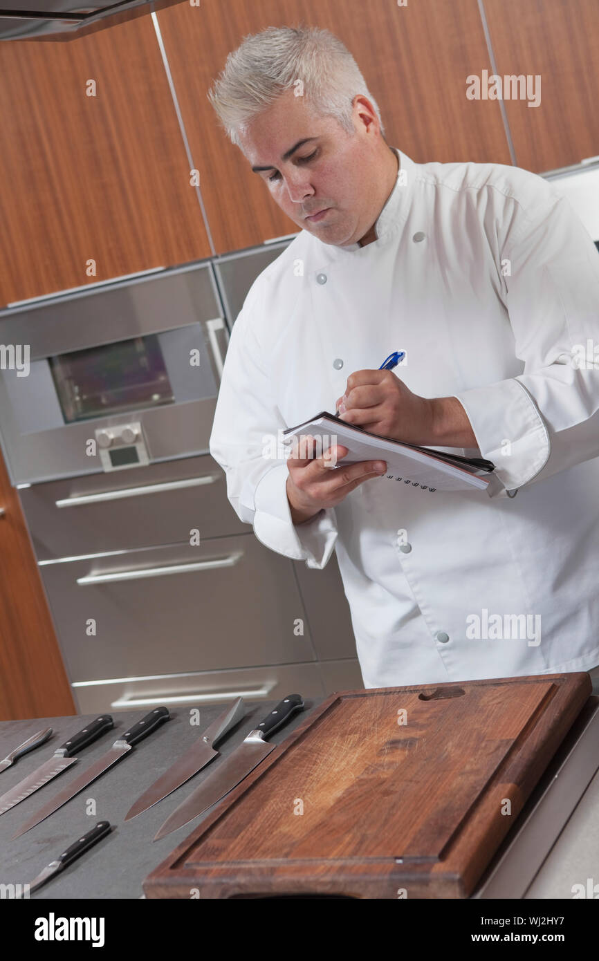 Male chef writing on notepad in commercial kitchen Stock Photo - Alamy