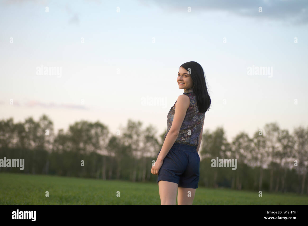 Happy young woman looking over shoulder while walking towards woodland ...