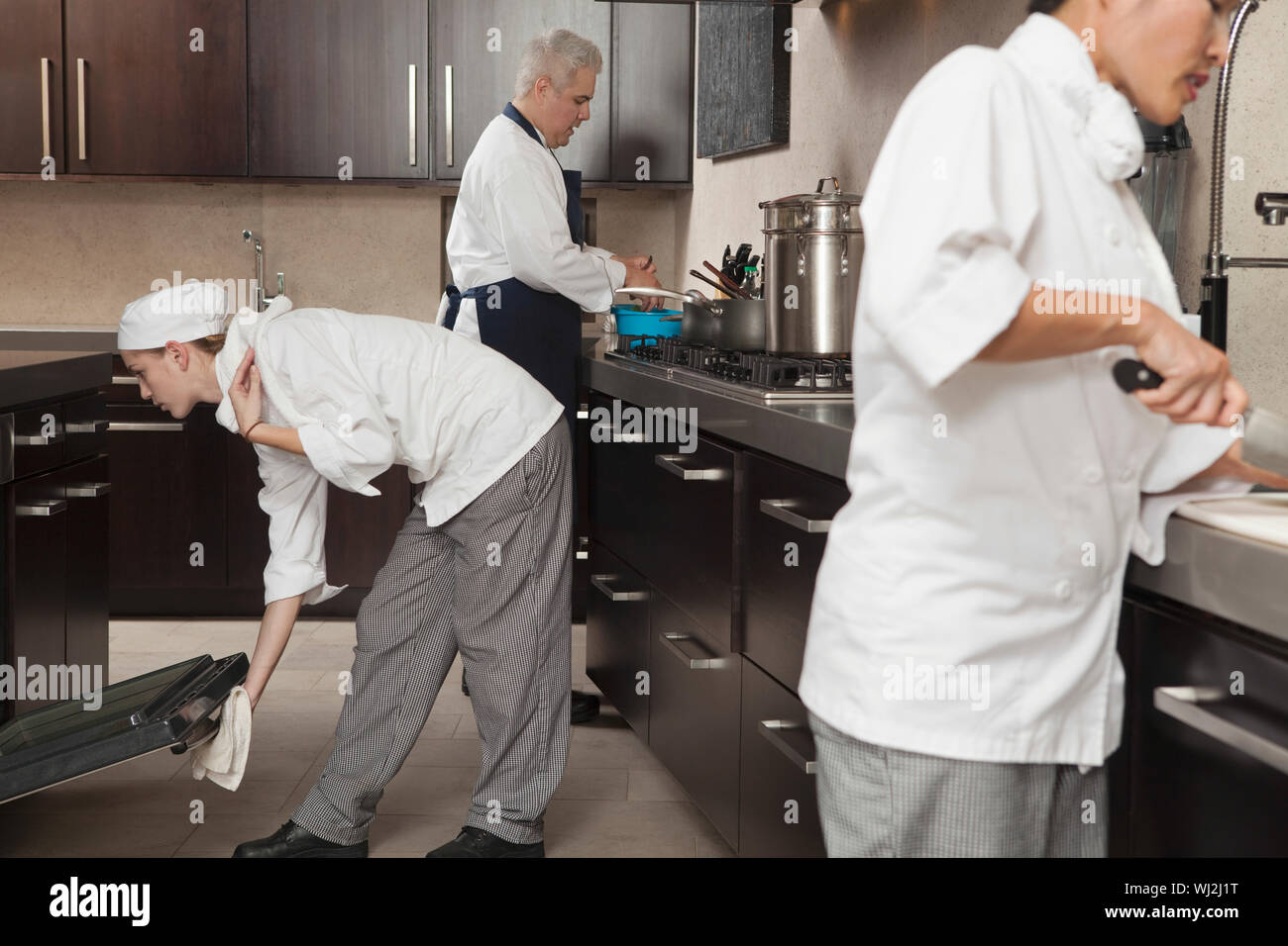 Three chefs working together in busy commercial kitchen Stock Photo - Alamy