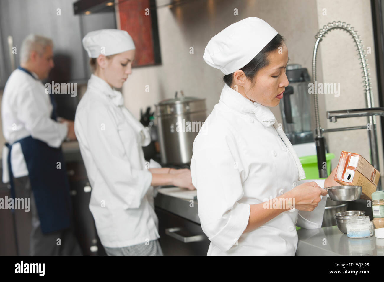 Three chefs working side by side in busy commercial kitchen Stock Photo ...