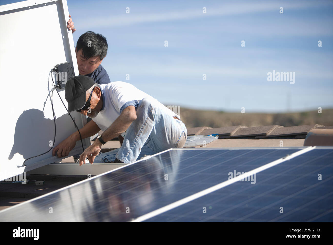 Male workers fixing solar panel on roof top against sky Stock Photo - Alamy