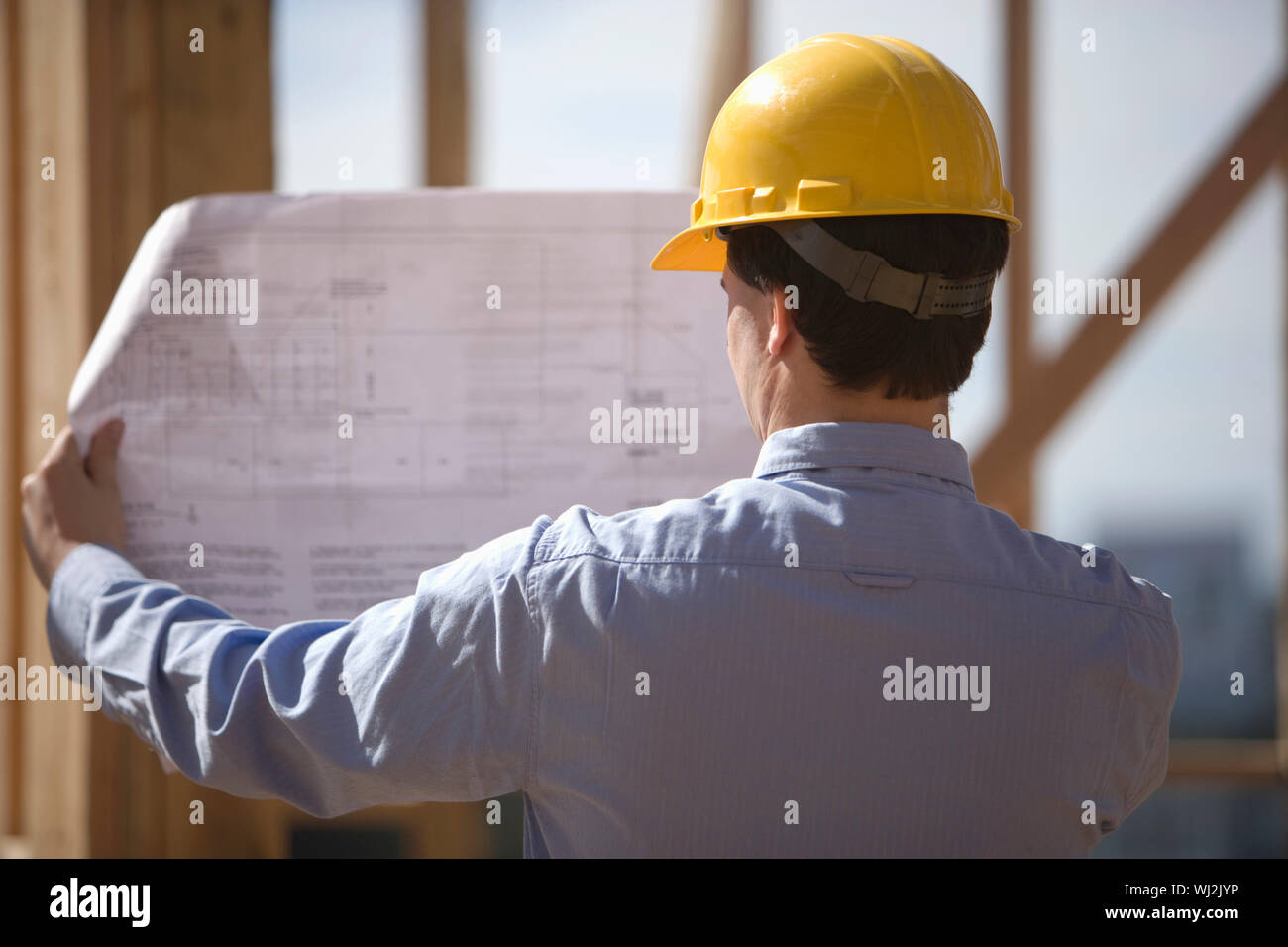 Rear view of a male architect holding blueprint at construction site ...
