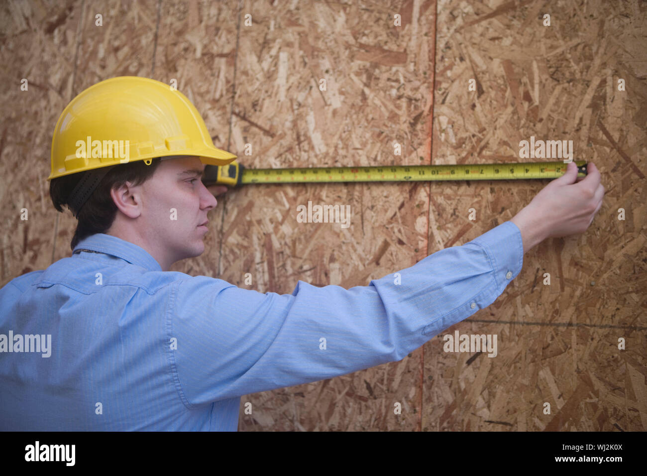 Young male architect measuring a wooden beam with measure tape at ...