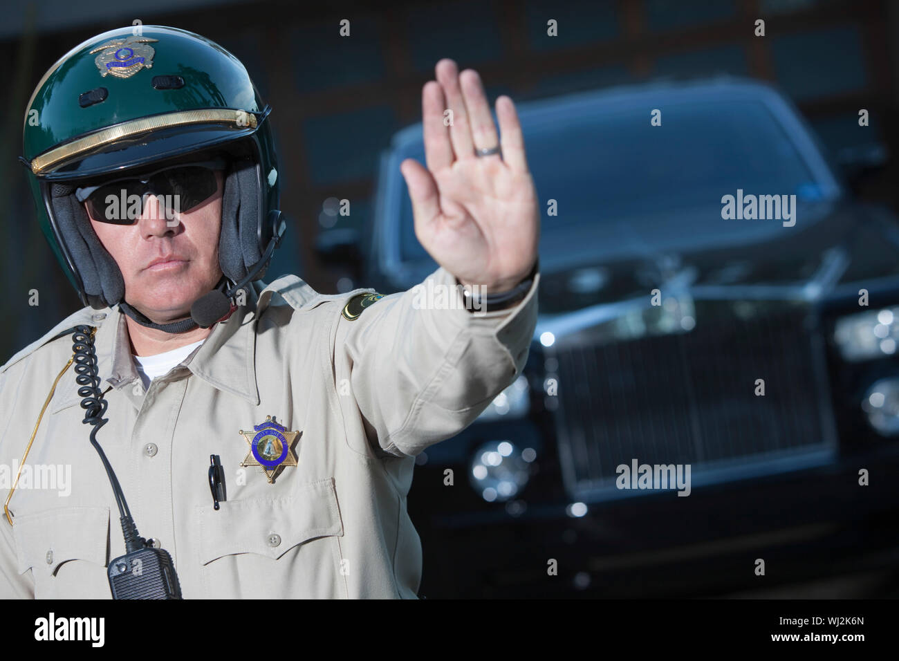 Confident middle aged traffic cop signaling stop gesture with car in ...