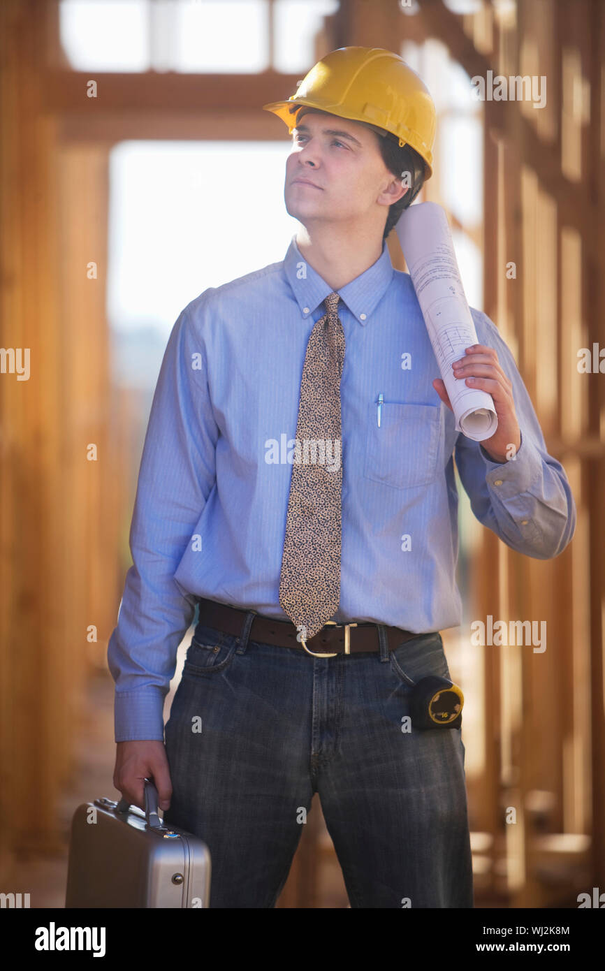 Confident Caucasian male architect holding briefcase with blueprint at ...