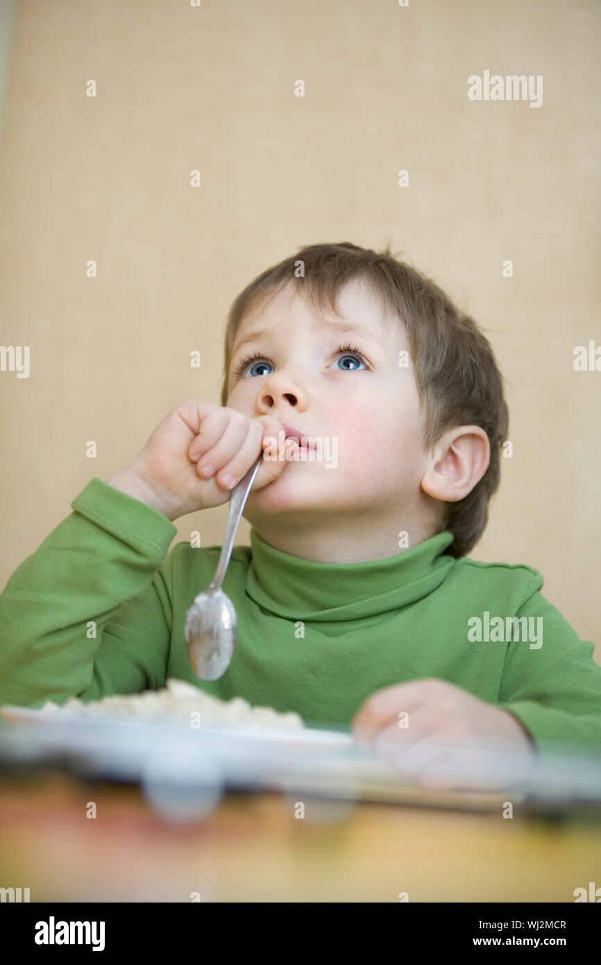 Cute little boy holding spoon while looking up at table in house Stock ...