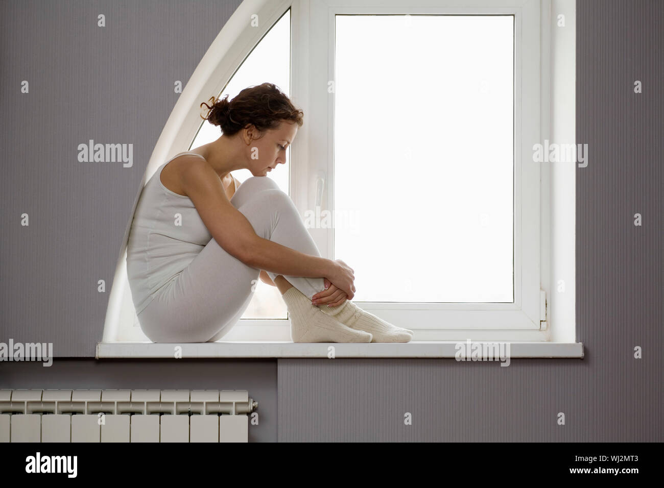 Profile shot of sad woman sitting on window sill Stock Photo - Alamy