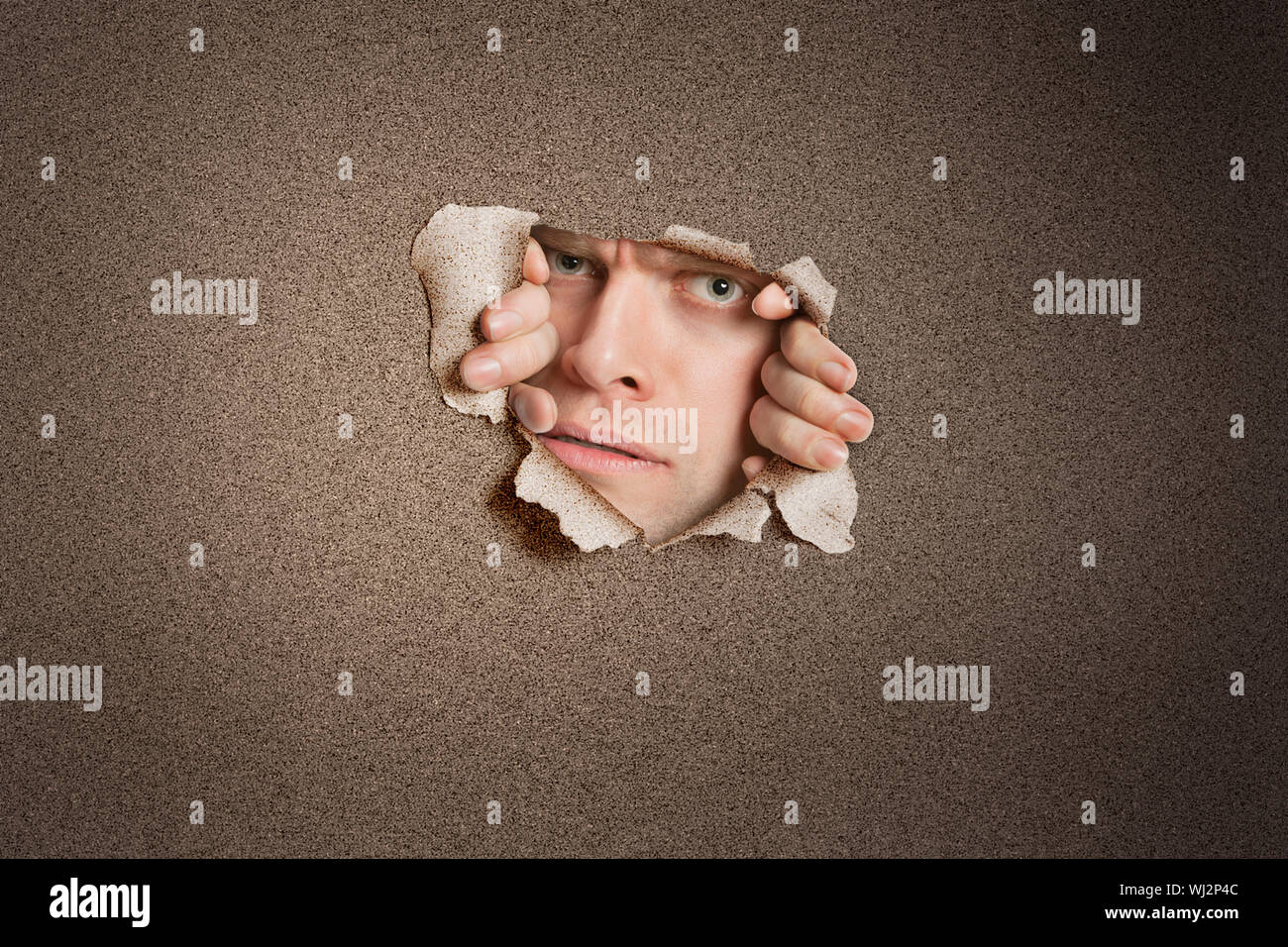 Portrait of a mid adult Caucasian man peeking from ripped white paper ...