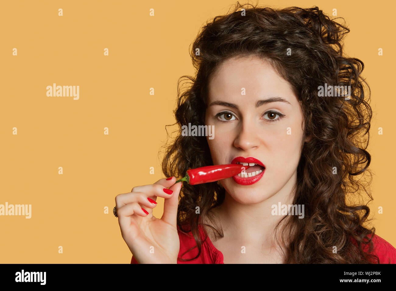Portrait of a young woman biting red chili pepper over colored ...