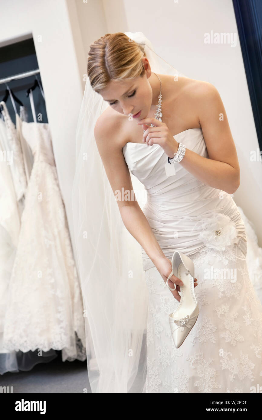 Beautiful confused woman in wedding dress holding footwear while ...