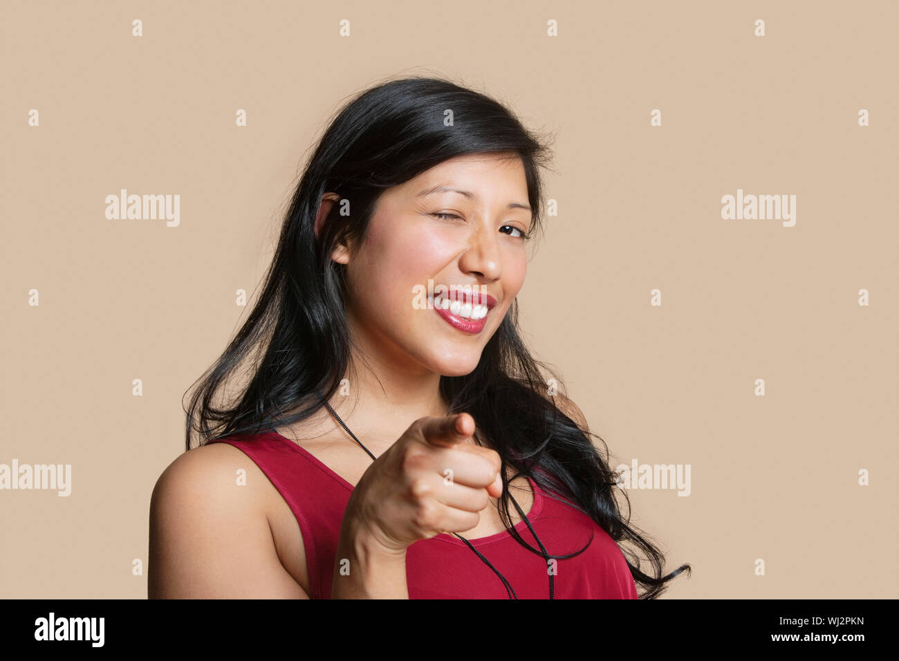 Portrait of a young woman pointing while winking over colored ...