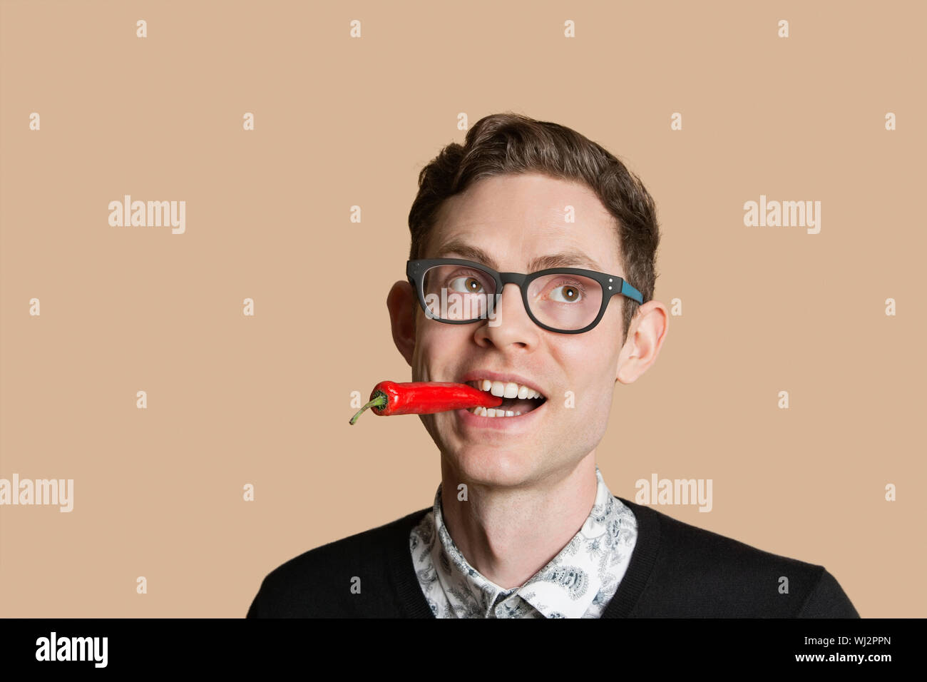 Mid adult man with red chili pepper while looking away over colored ...