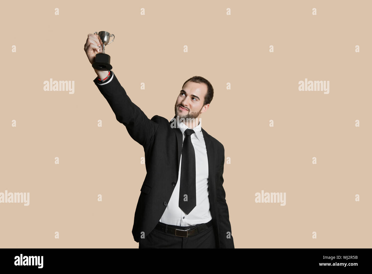 Happy young man raising winning trophy over colored background Stock ...