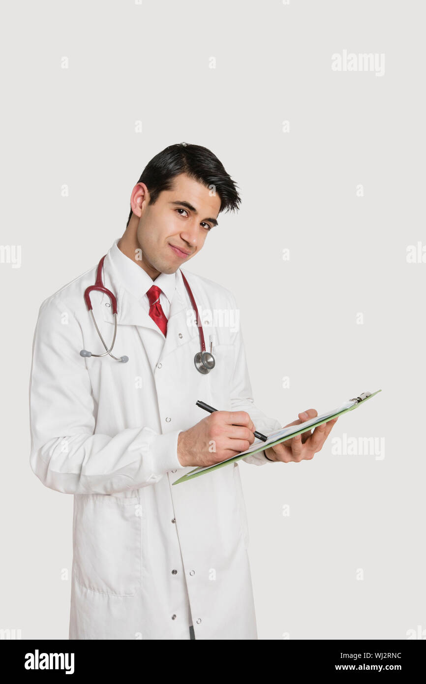 Portrait of an Indian male doctor writing prescription over light gray ...