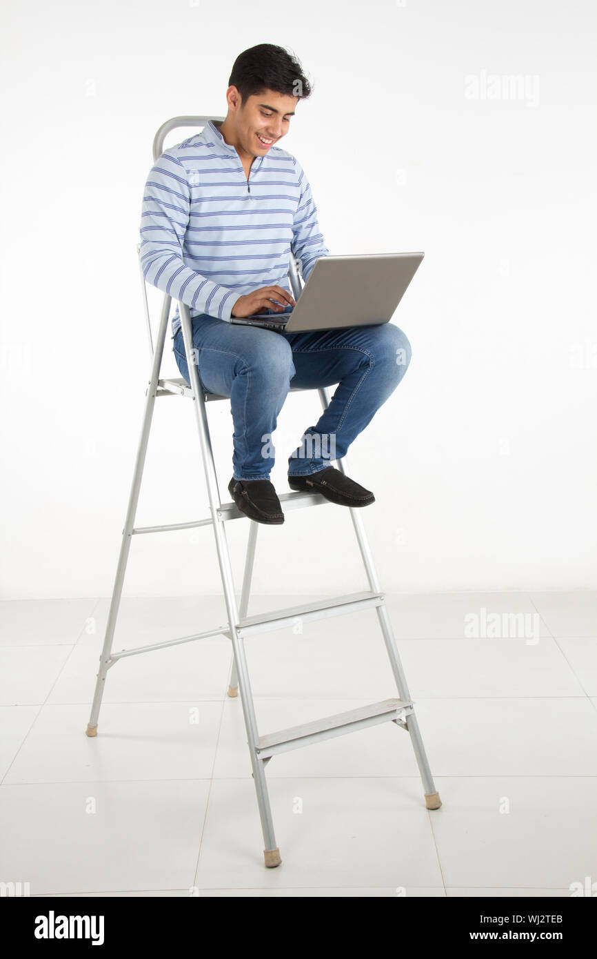 Young man sitting on a step ladder using a laptop Stock Photo - Alamy
