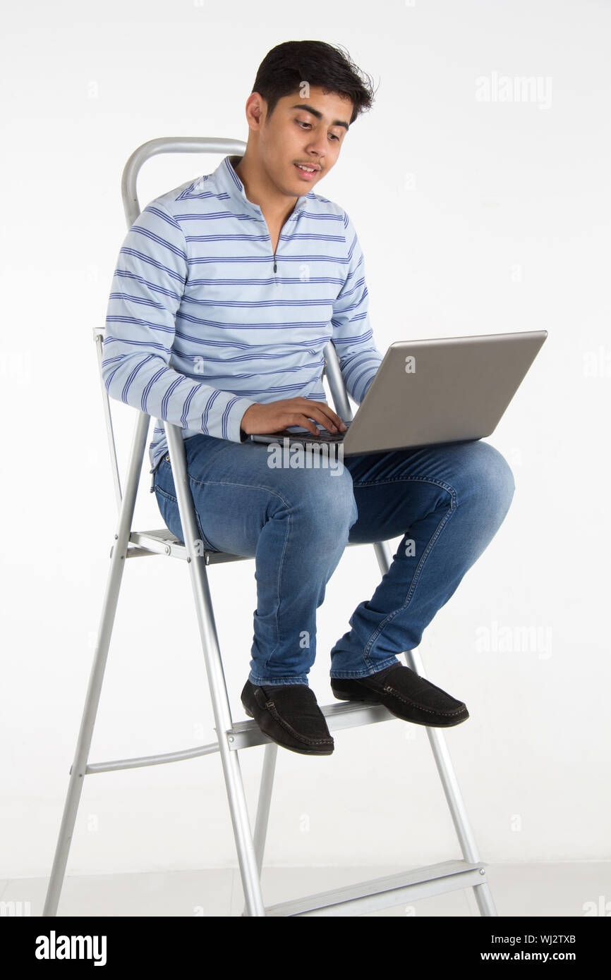 Young man sitting on a step ladder using a laptop Stock Photo - Alamy
