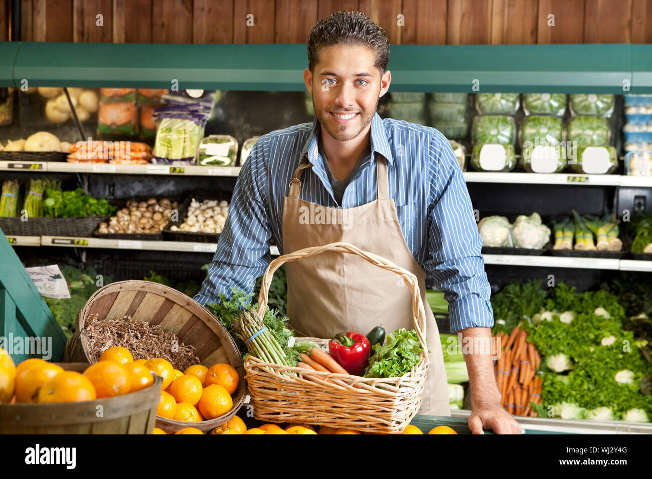 Portrait of a happy young salesman with vegetable basket in supermarket ...