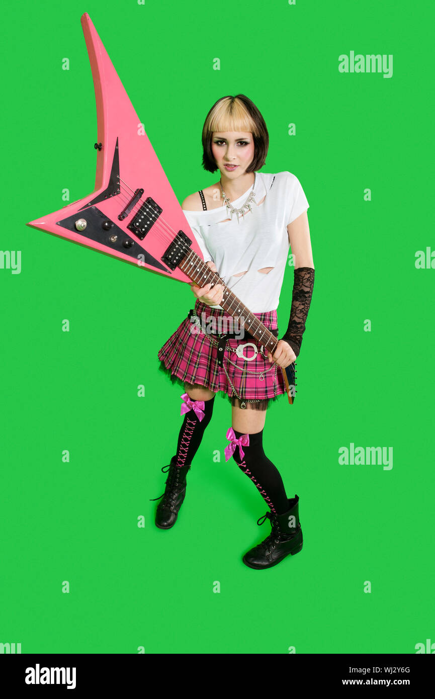 Beautiful punk woman with guitar over green background Stock Photo - Alamy