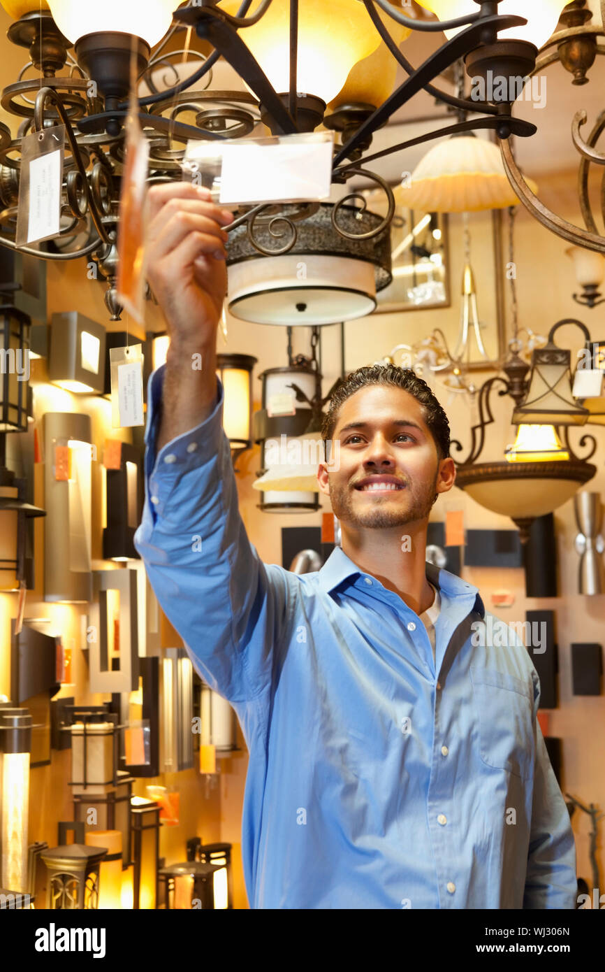 Happy young man looking at price tag of chandelier in lights store ...
