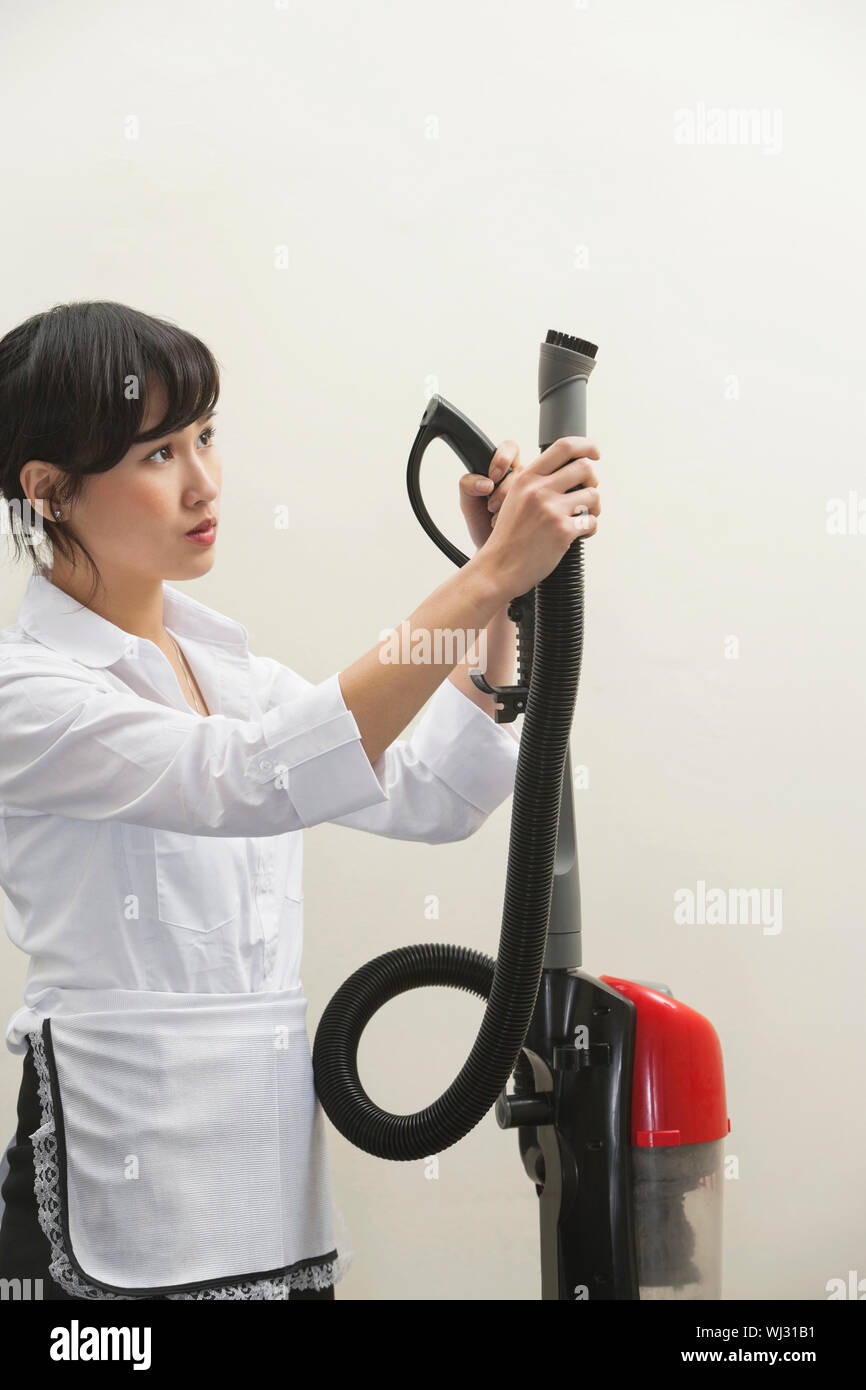 Female housekeeper holding vacuum cleaner pipe against gray background ...