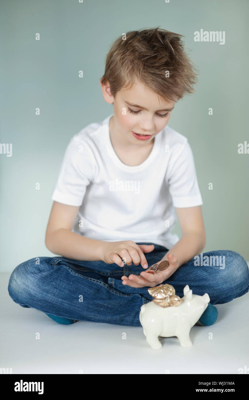 Boy with piggy bank counting coins over gray background Stock Photo - Alamy