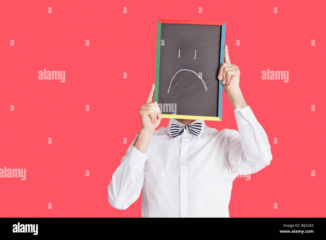 Man holding sad smiley face sign over red background Stock Photo - Alamy